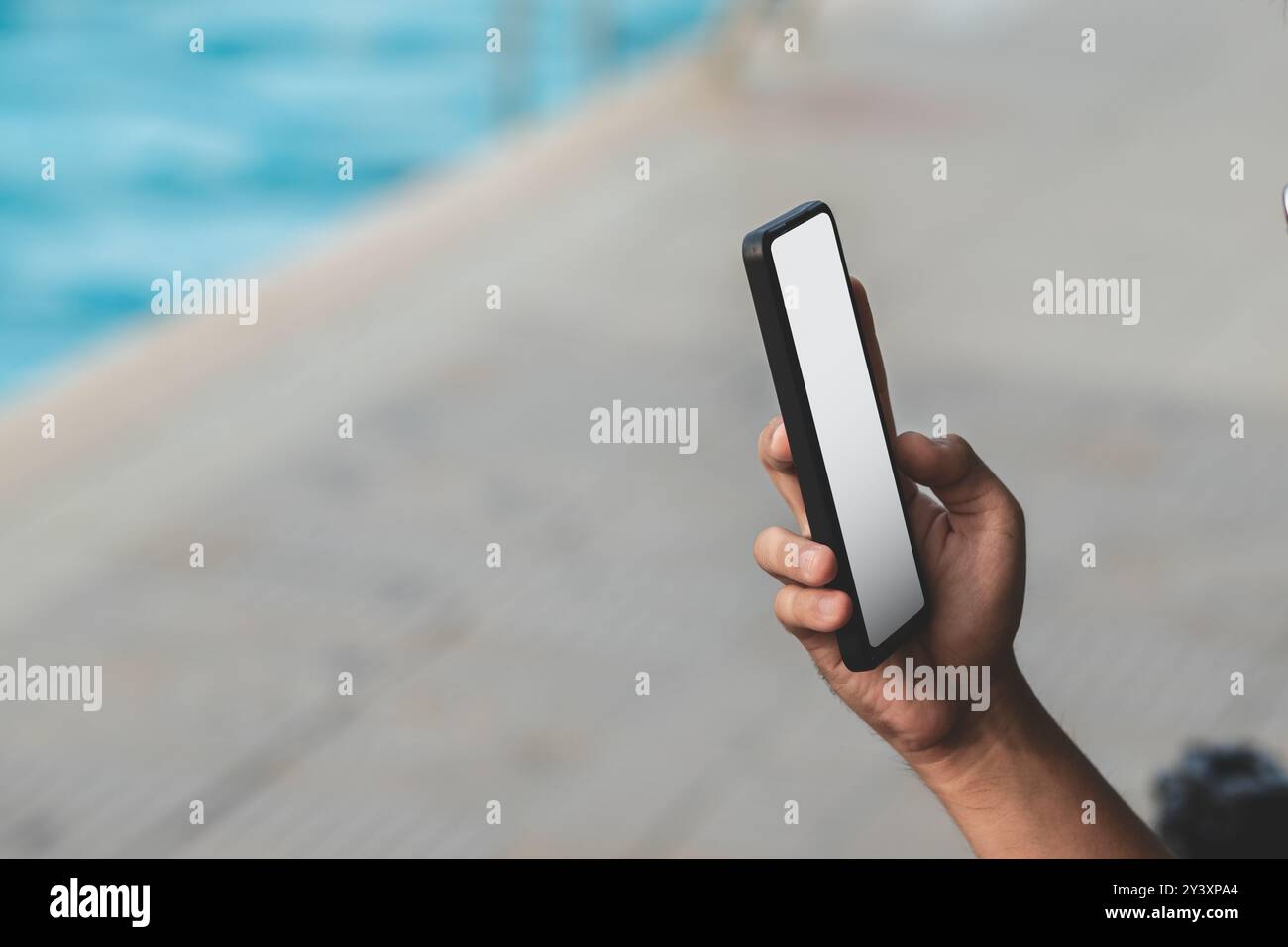 Hand holding phone with one hand beside swimming pool. Typing on white ...