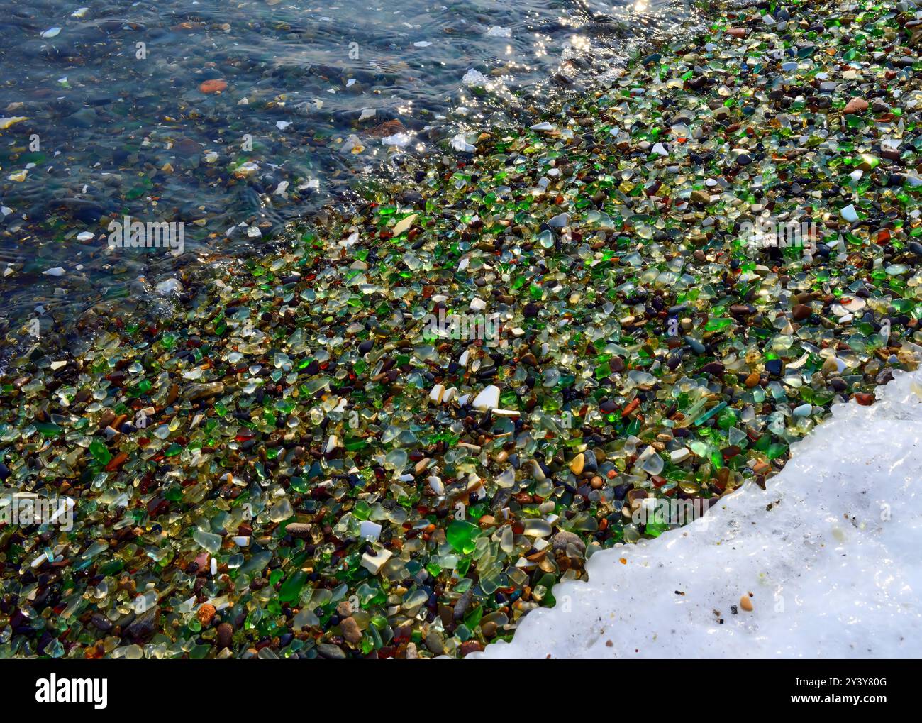 Multi-colored glass on the ice and snow of Japanese sea. Glass beach ...