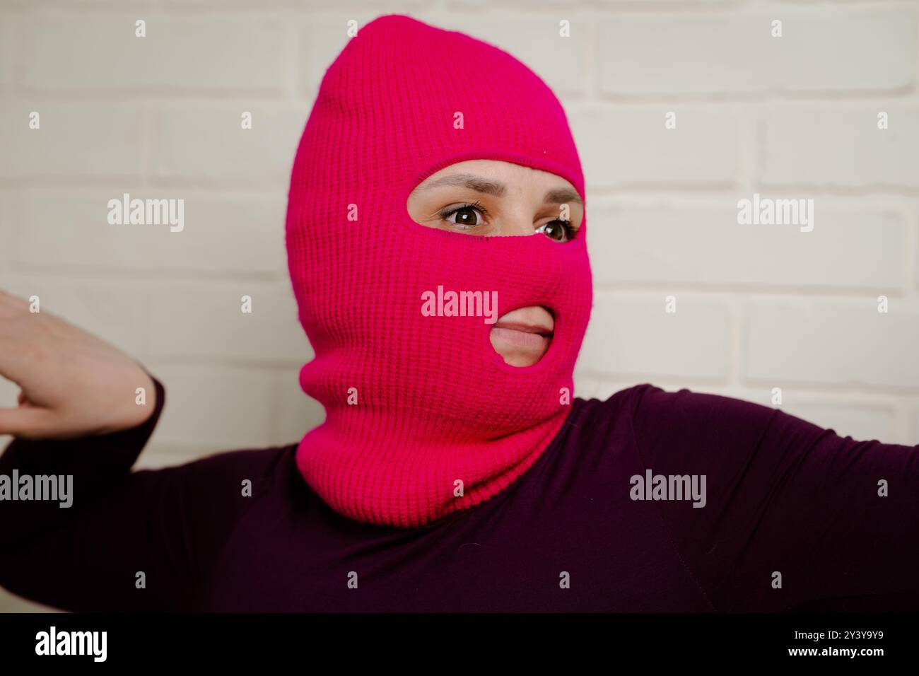 A woman wearing a bright pink balaclava dances energetically, striking ...