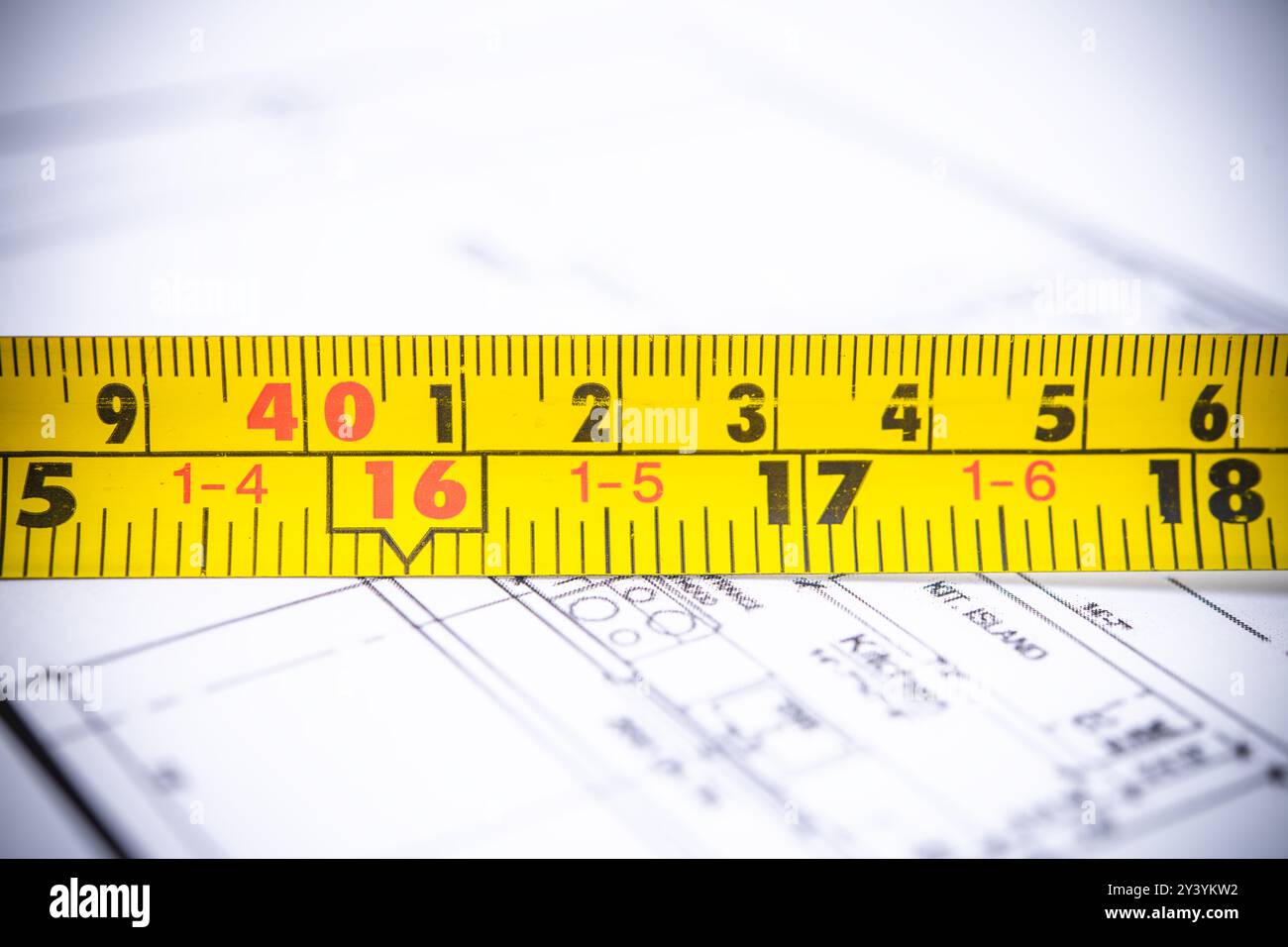 Yellow measuring tape aligns with construction blueprints, emphasizing ...