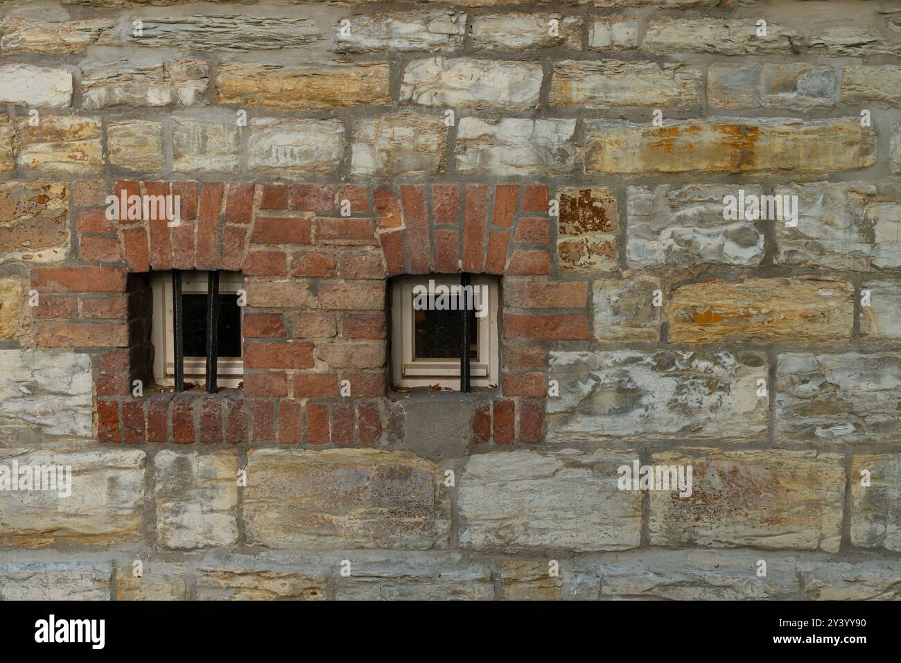 The brick and stone wall features two small barred windows, showcasing ...
