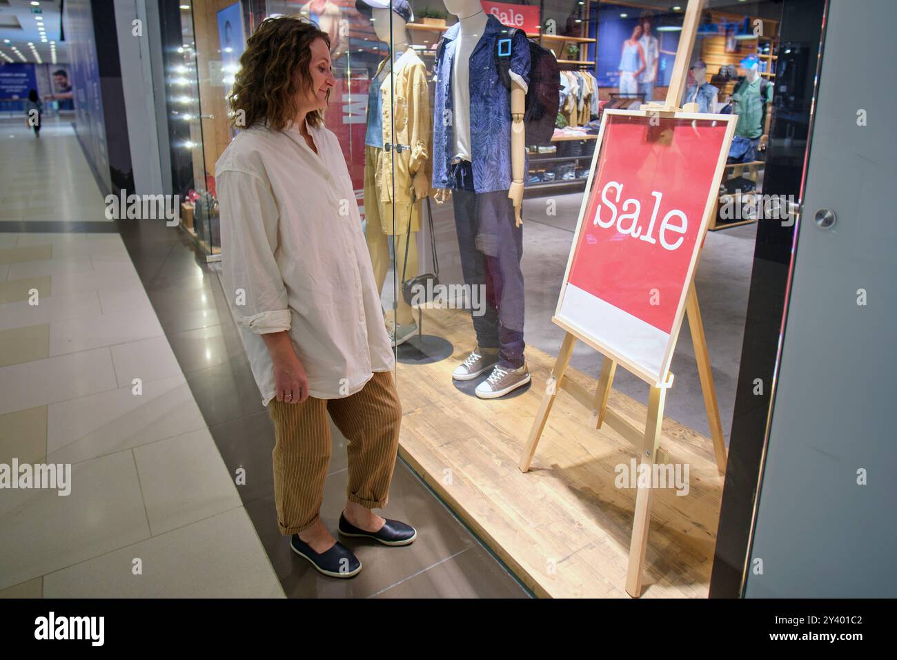 Woman looking at shop window display with 'Sale' sign in shopping mall ...