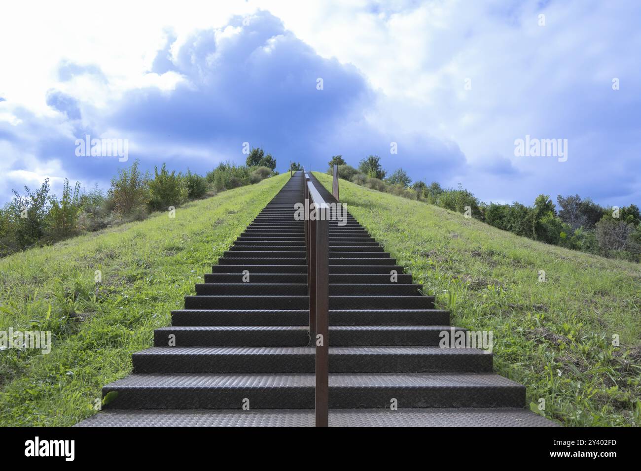 Steep metal stairs, brown, railing in the centre, green meadow to the ...