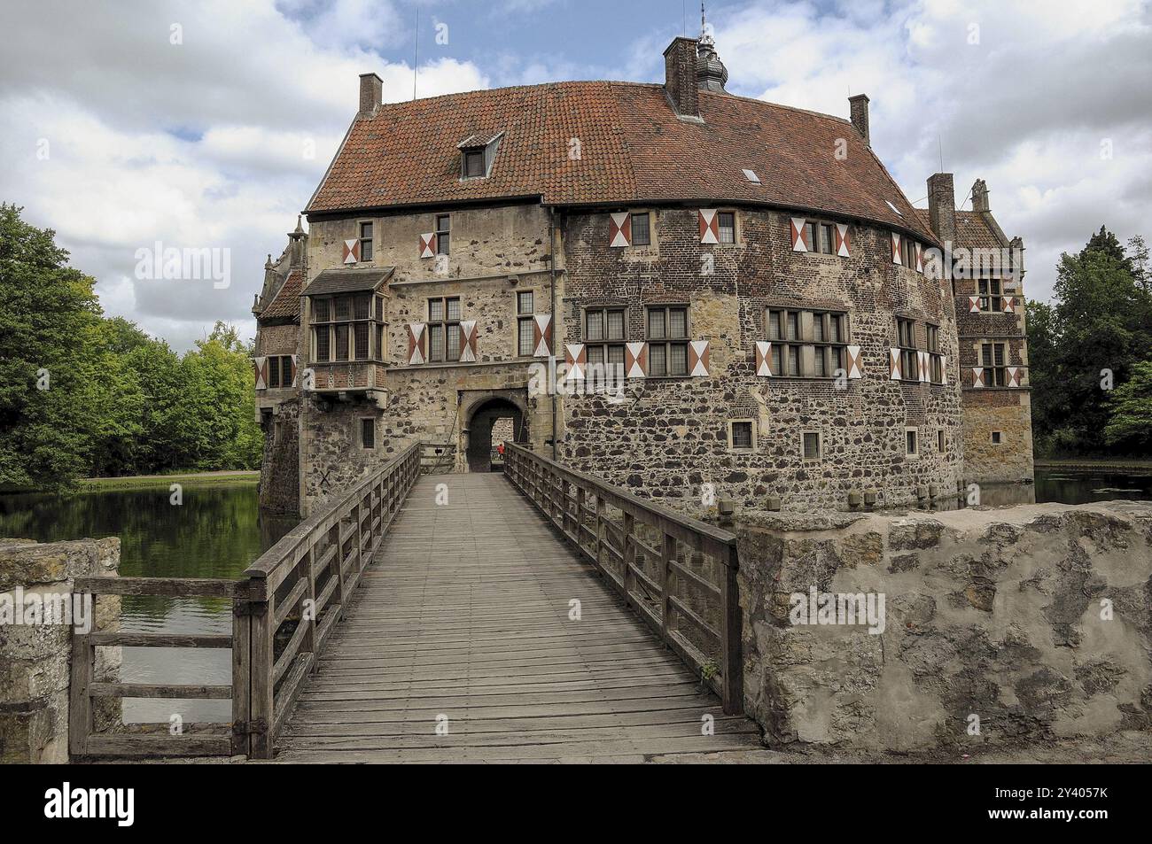 Wide bridge leads to a historic castle with moat, surrounded by nature ...