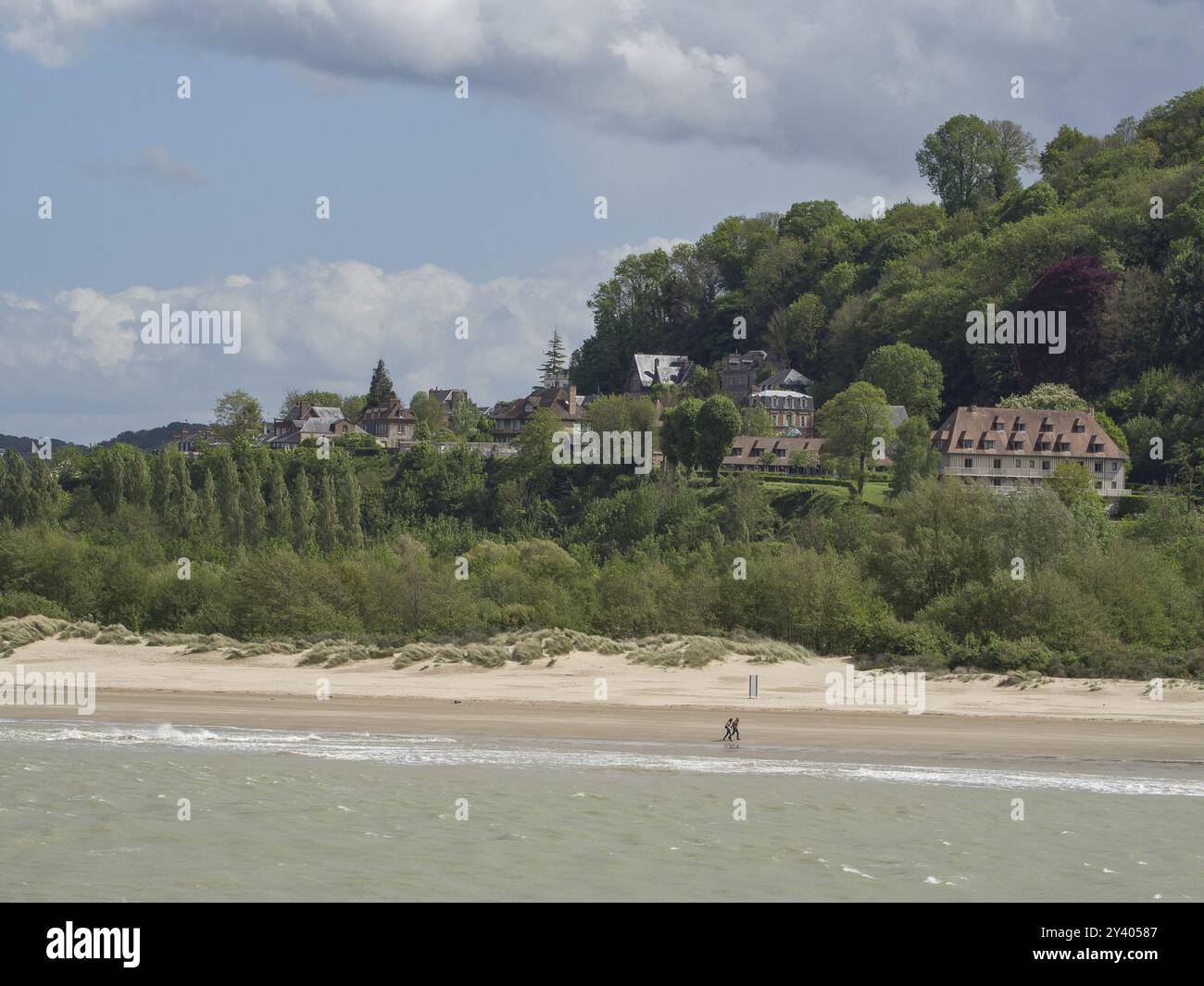 A village stretches along a hill with houses in front of a quiet beach ...
