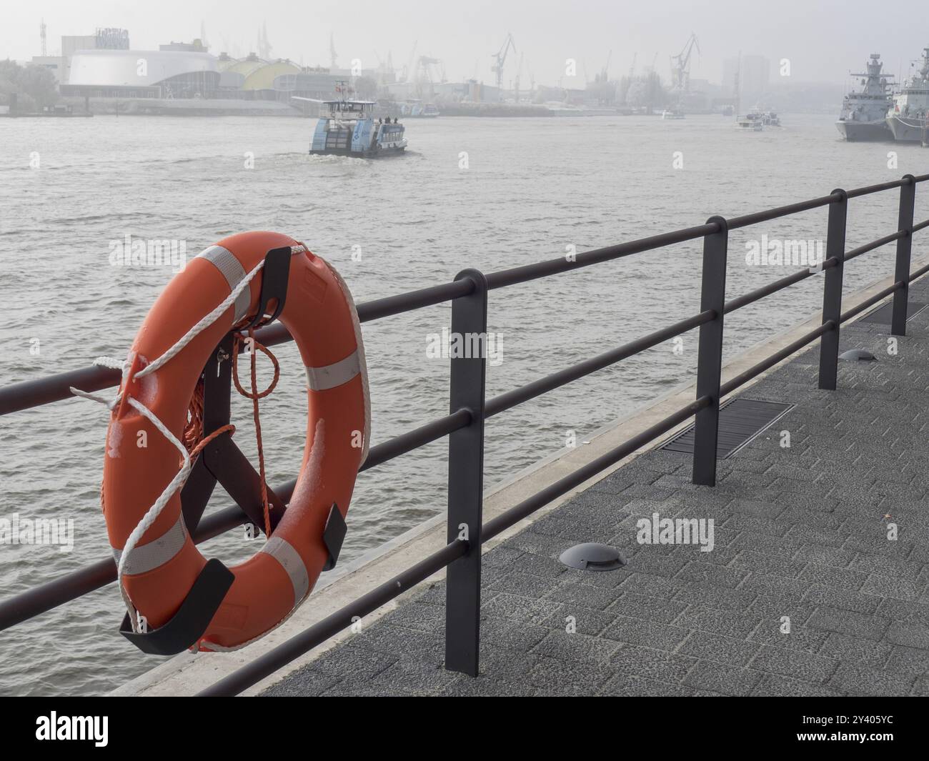 Lifebuoy on the railing along a river. Boats in the background in foggy ...