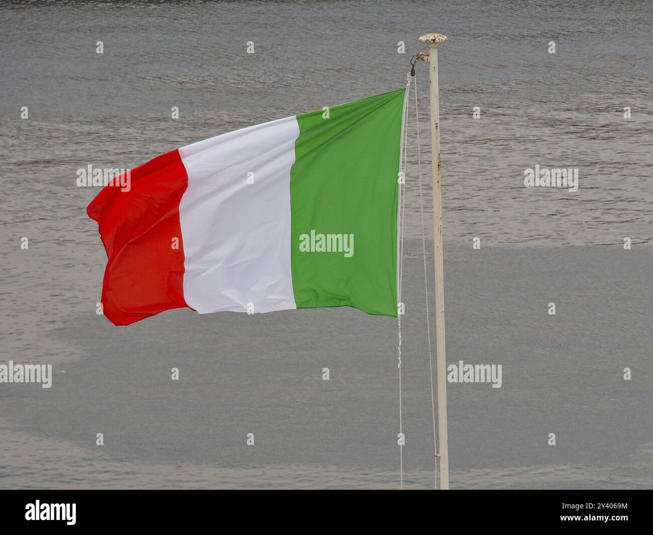 Italian flag waving in the wind in front of a body of water, naples ...