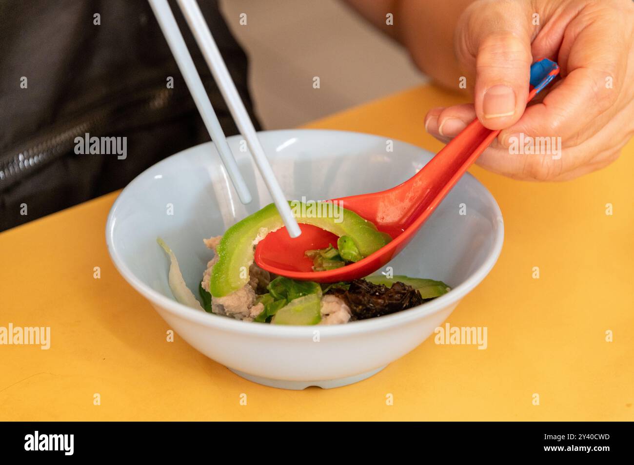A Chinese diner using chopsticks in the Chinatown Complex filled with ...