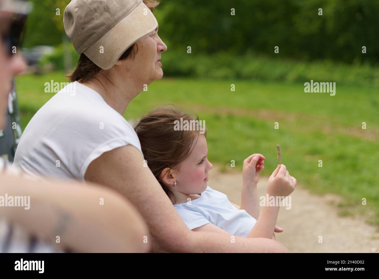 A cute little girl sits on a bench in her grandmother's arms in a ...