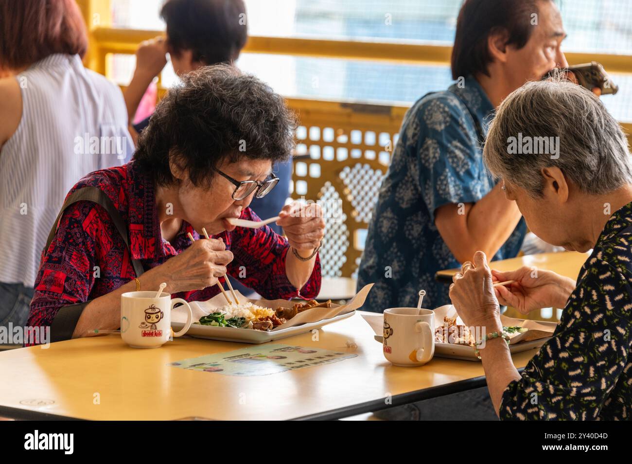 A Chinese diner using chopsticks in the Chinatown Complex filled with ...