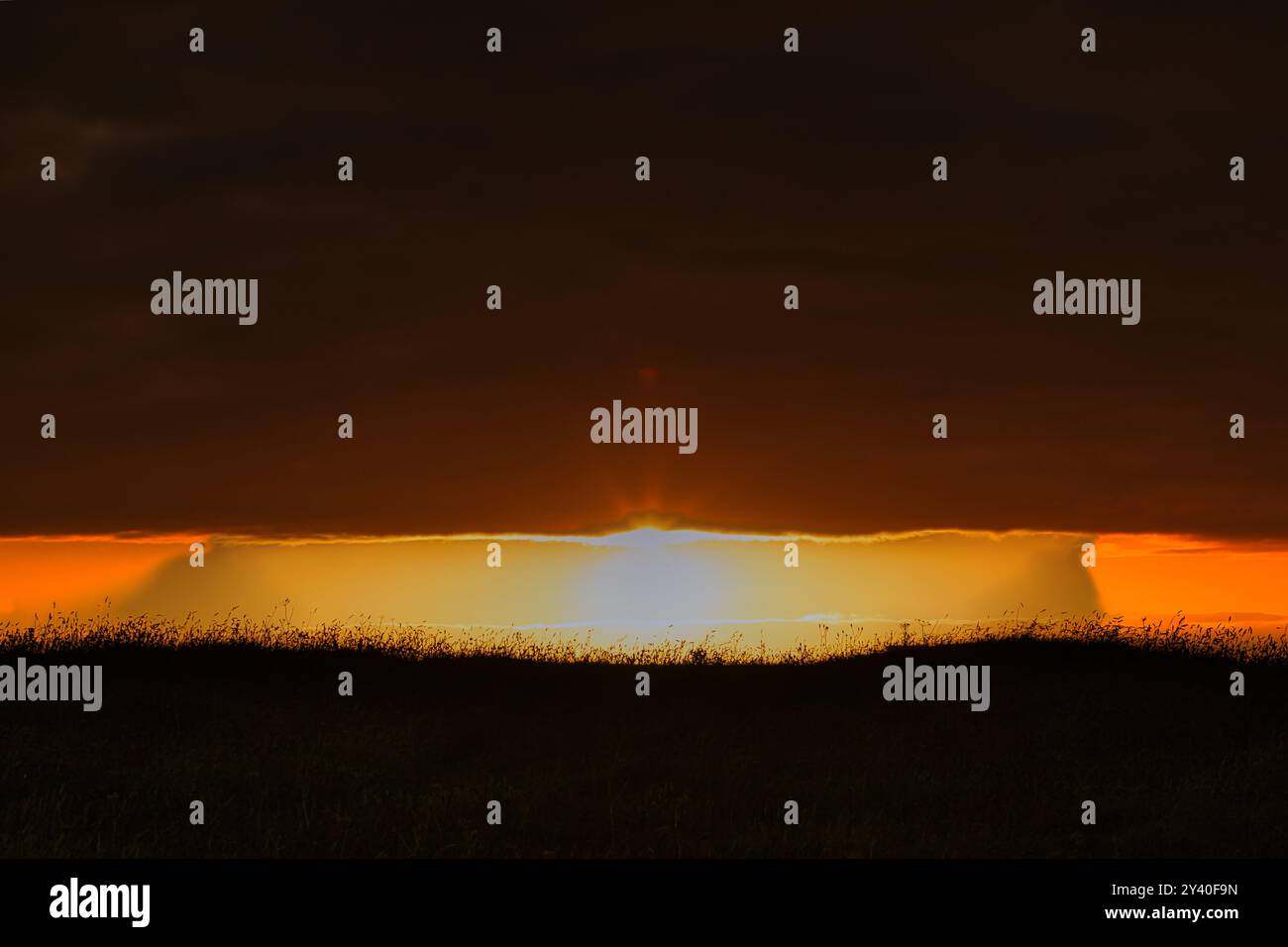 A stunning sunset scene with a dark cloud cover above a glowing horizon ...