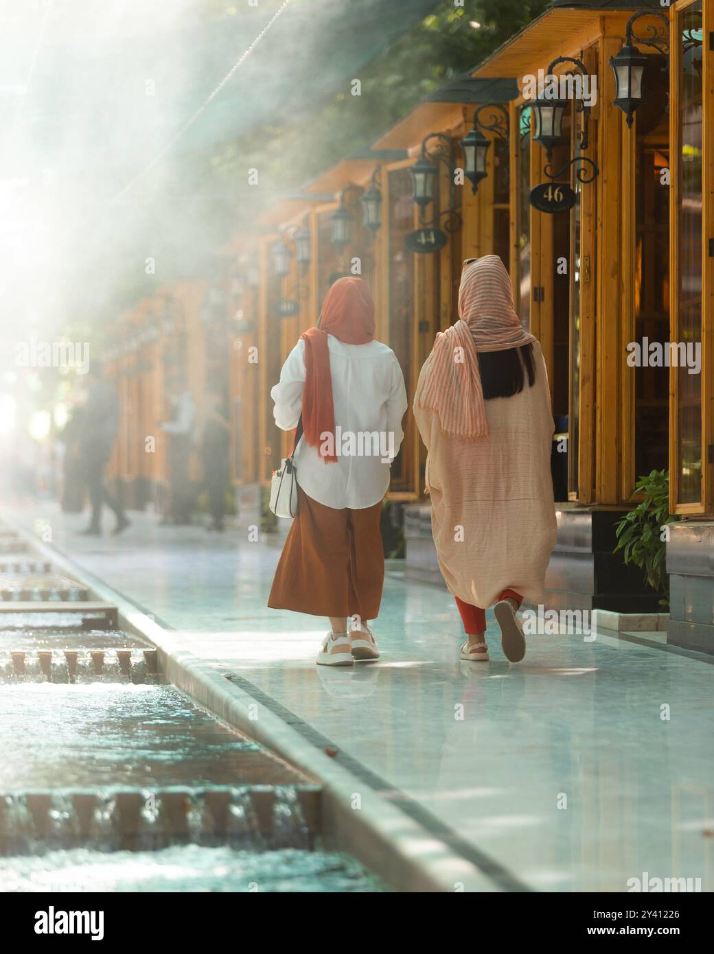 Two women in traditional attire walking along a misty path near cozy ...