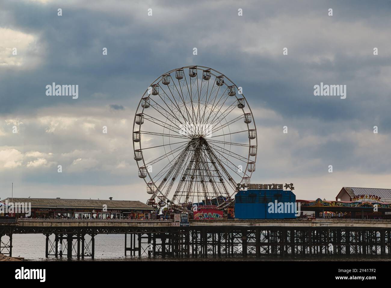 A large Ferris wheel stands on a pier, surrounded by amusement rides ...