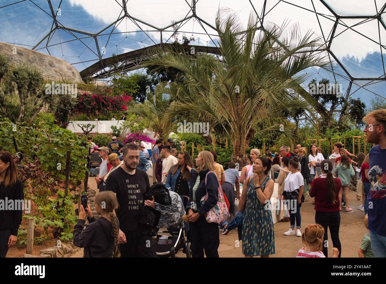 A bustling indoor garden with a diverse crowd of people exploring lush ...