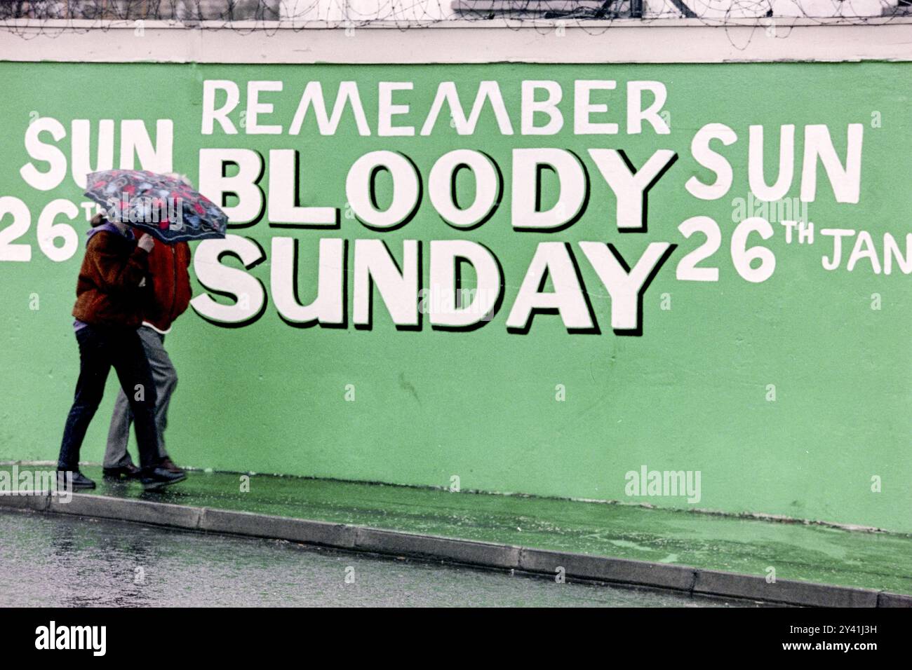 A couple walks past a mural during a rainy day in the Bogside area ...