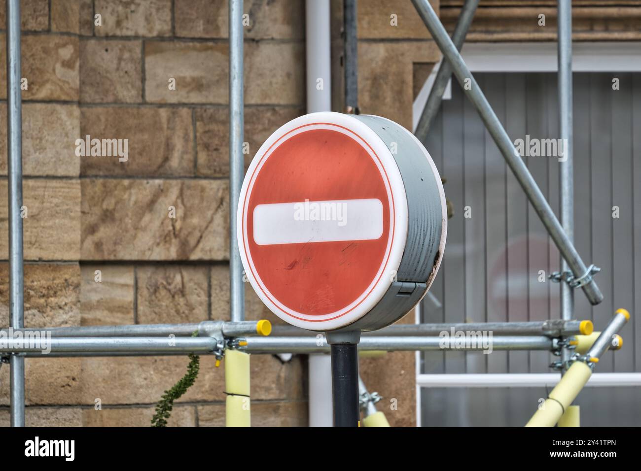A red no entry sign mounted on a pole, surrounded by scaffolding and a ...