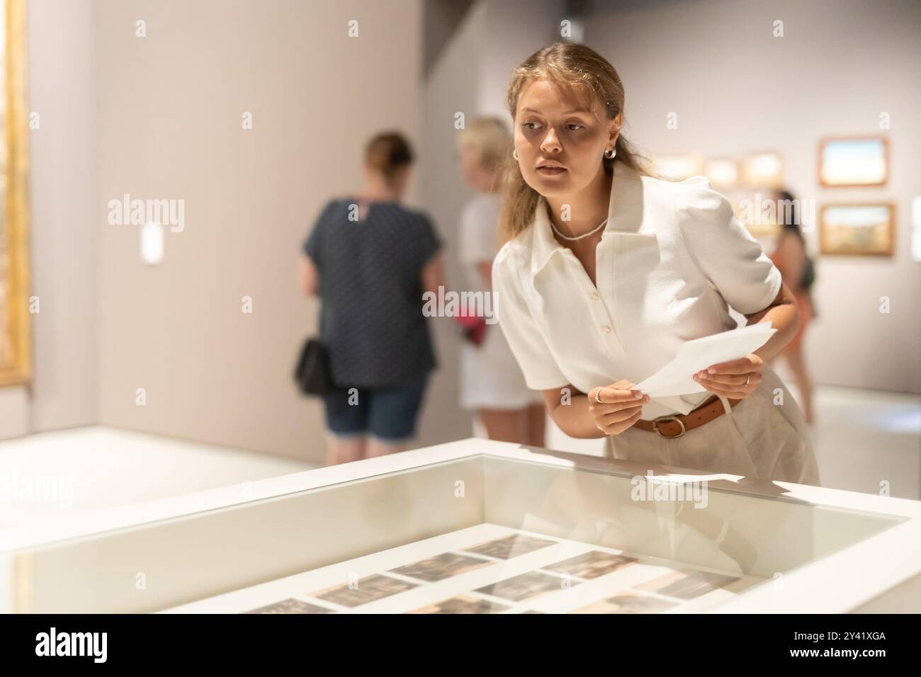Young female visitor stands near glass display case and examines ...