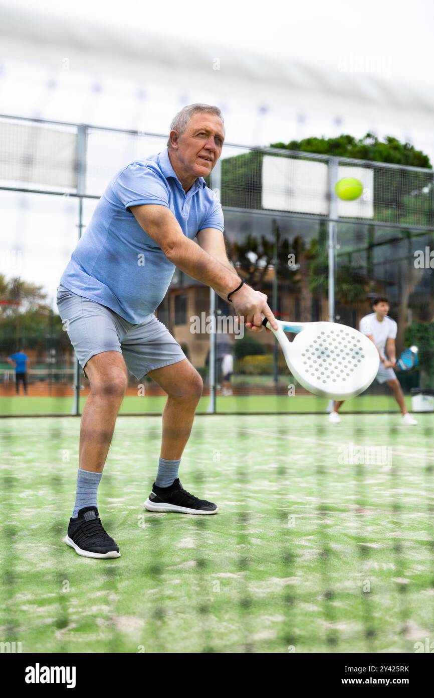 European old man holding playing padel during training in court. View ...