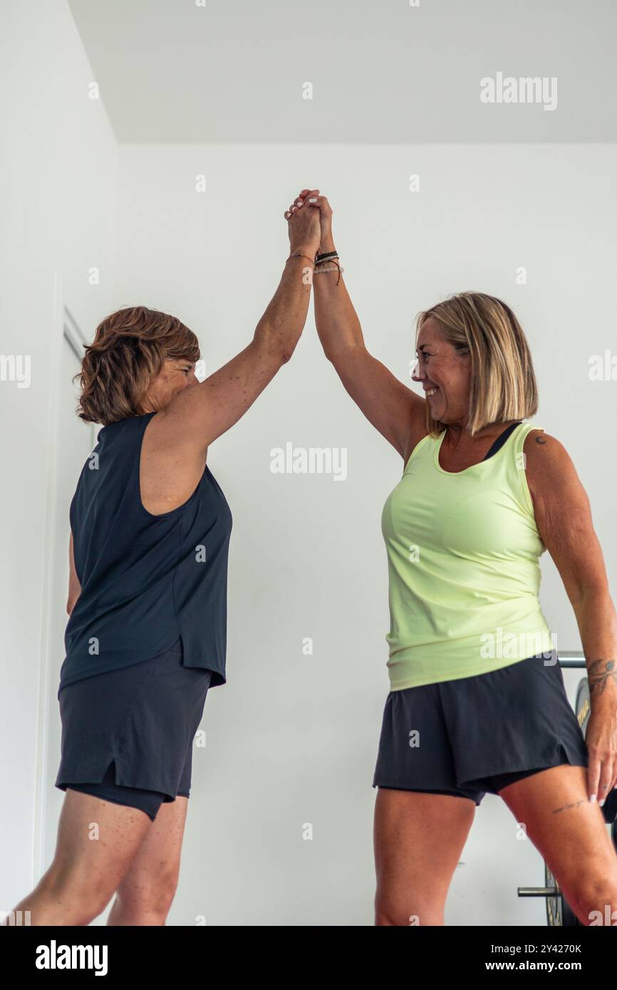 vertical Two mature women in sportswear are celebrating by high-fiving ...