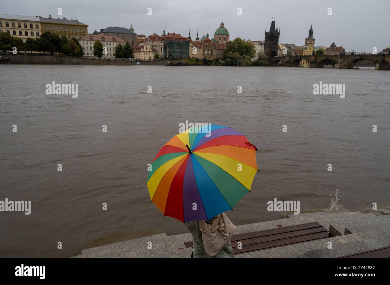 A woman with rainbow umbrella observes the rising water level of Vltava ...