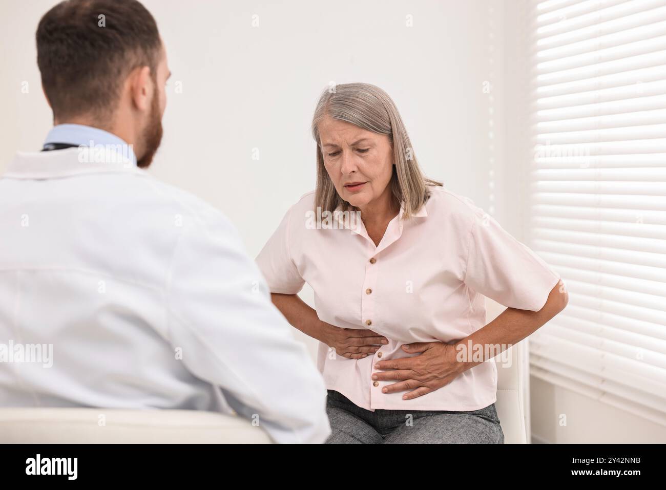 Doctor consulting senior patient with stomach pain in clinic, back view ...