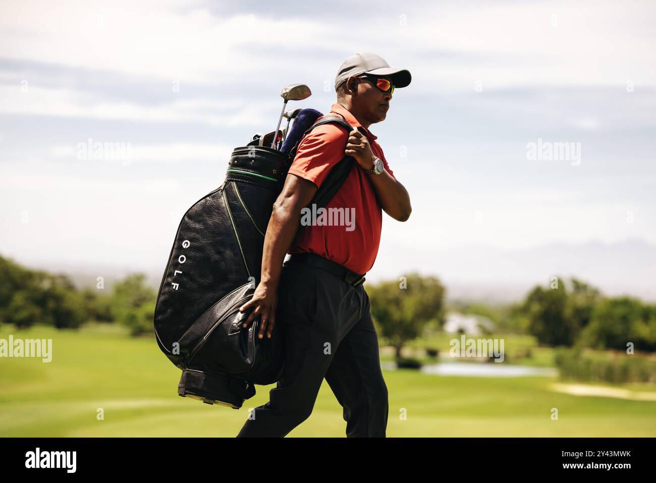 Golf caddy carrying a golf bag on the fairway, wearing a cap, walking ...