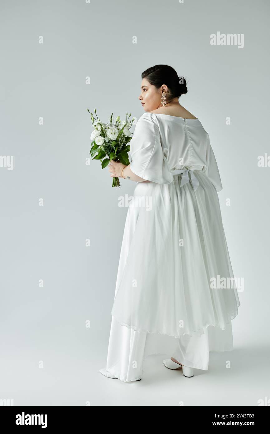 A beautiful plus size bride stands gracefully in a flowing white gown ...