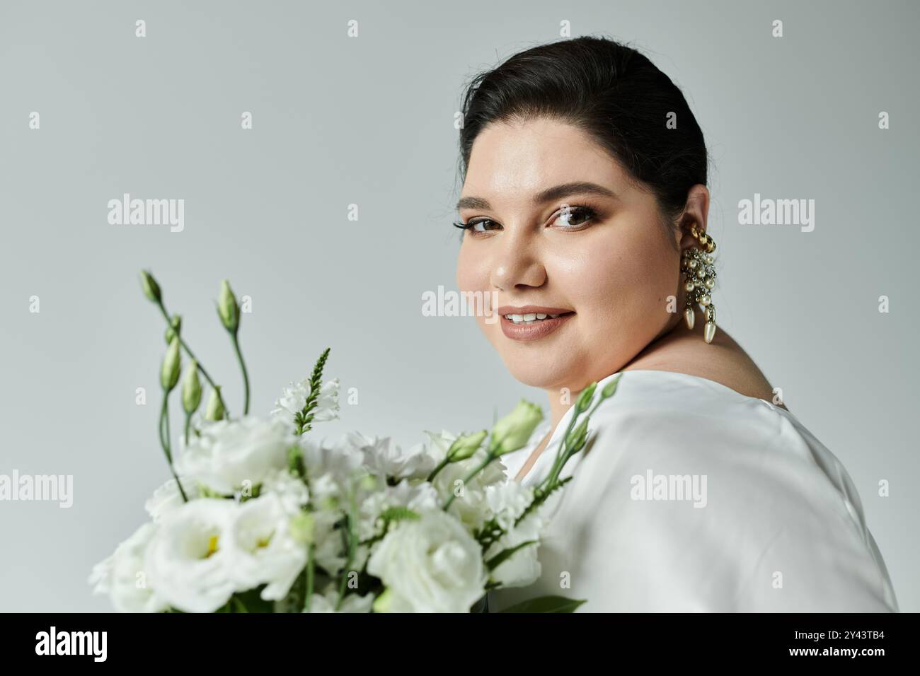 A beautiful plus size bride smiles softly while holding a bouquet ...