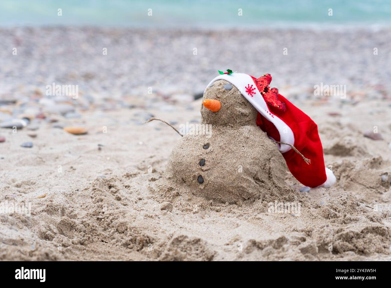 Snowman with Santa hat made with beach sand on the seashore with copy ...