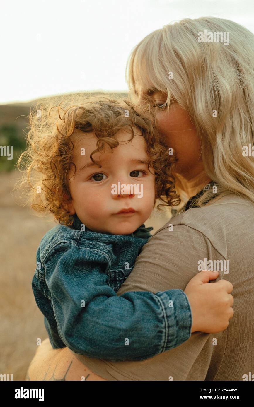 Blonde mom snuggles baby with brown curly hair in the mountains Stock ...