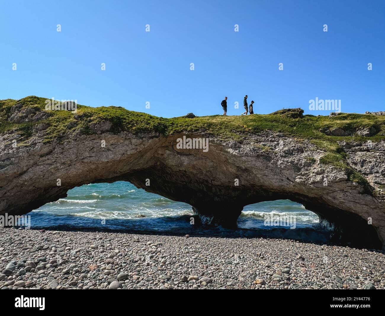 People walking across natural rock arches on beach in Newfoundland ...