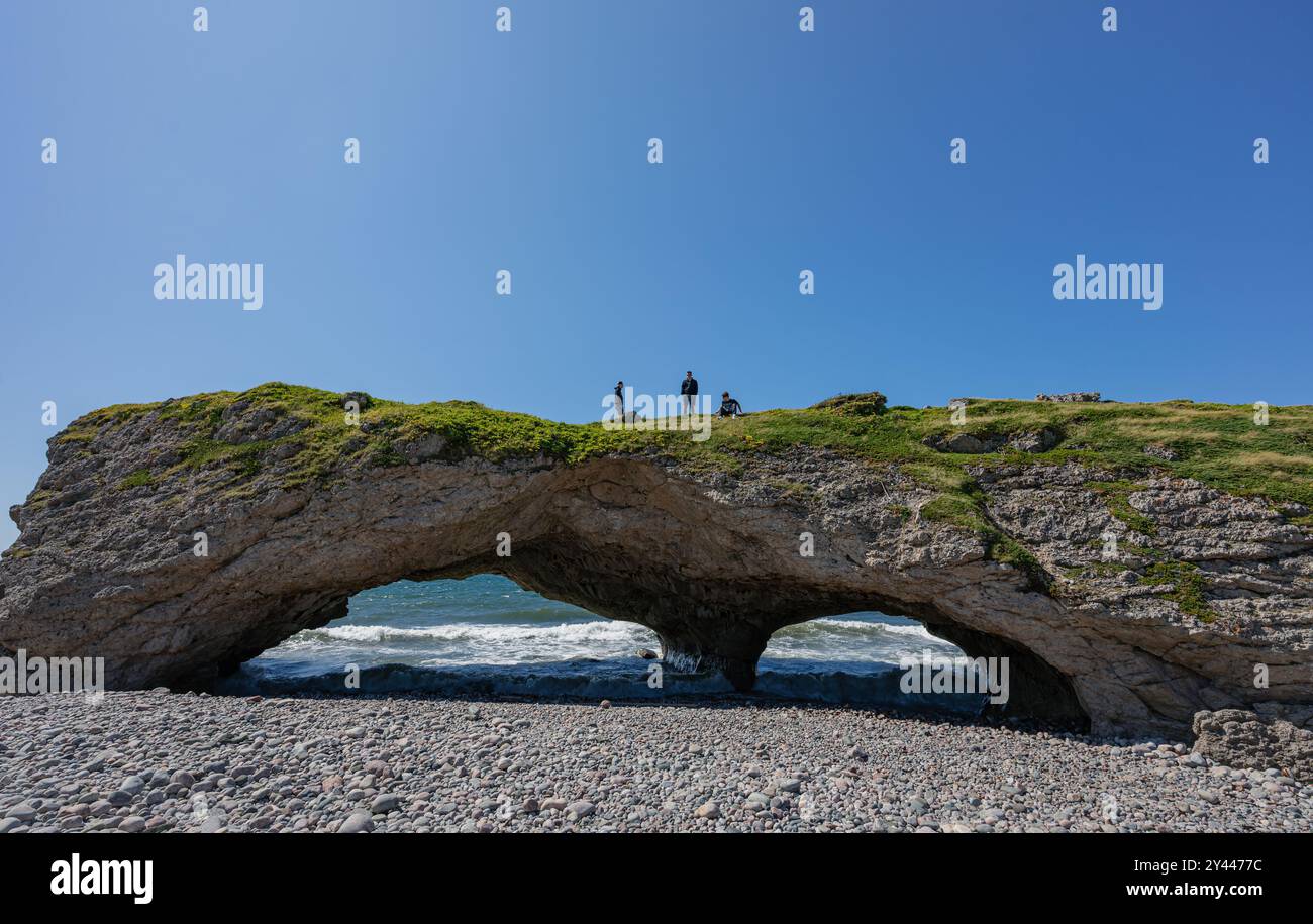Three people atop natural rock arches on beach in Newfoundland Stock ...