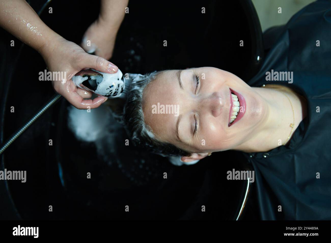 Client smiling while enjoying a foamy hair wash at the salon si Stock ...