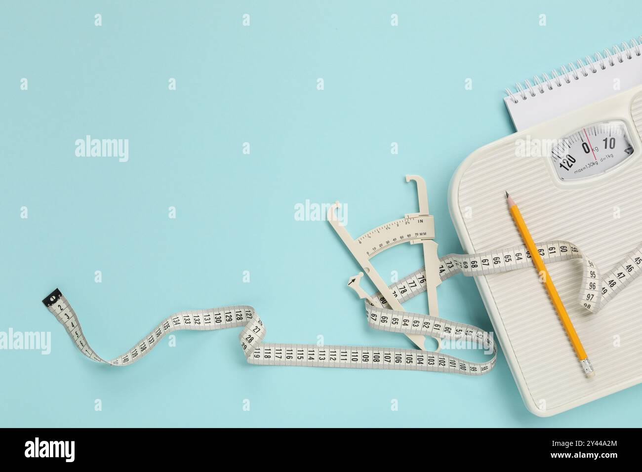 Body fat caliper, measuring tape, scale, pencil and notebook on light ...