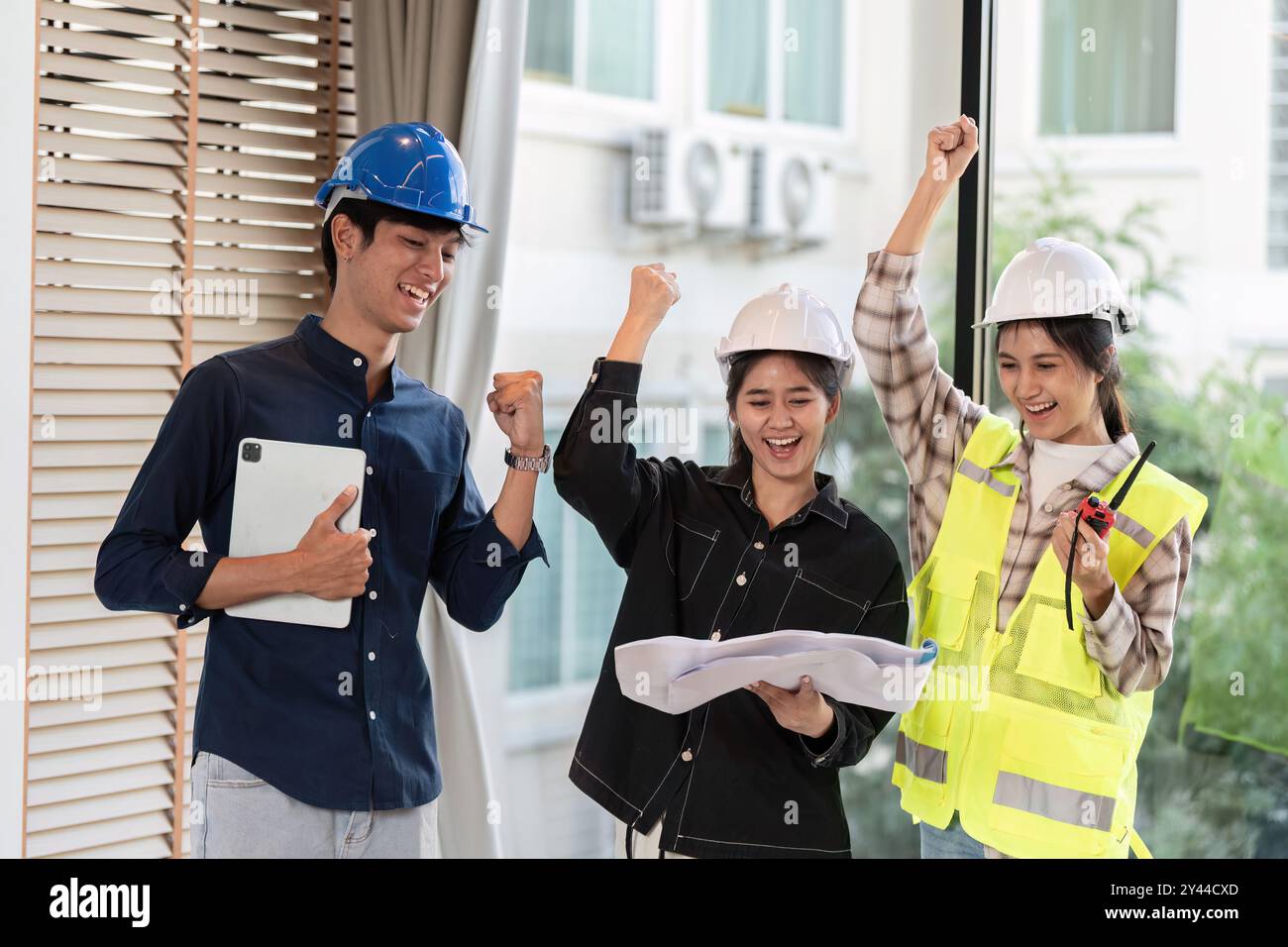 Group of Happy Engineers Celebrating Success at Construction Site with Blueprints and Safety ...