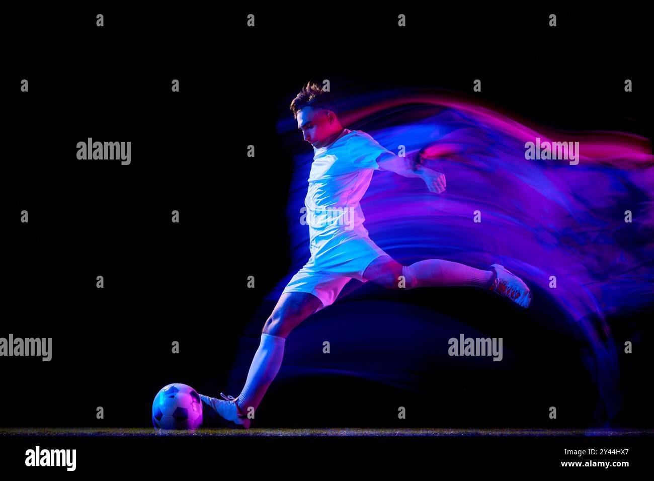 Focused football player, dressed in white under neon lighting, performs ...