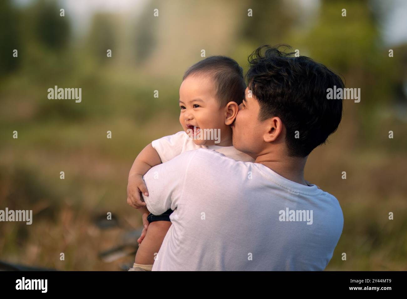 A baby boy is being hugged by a father while smiling and the father is ...
