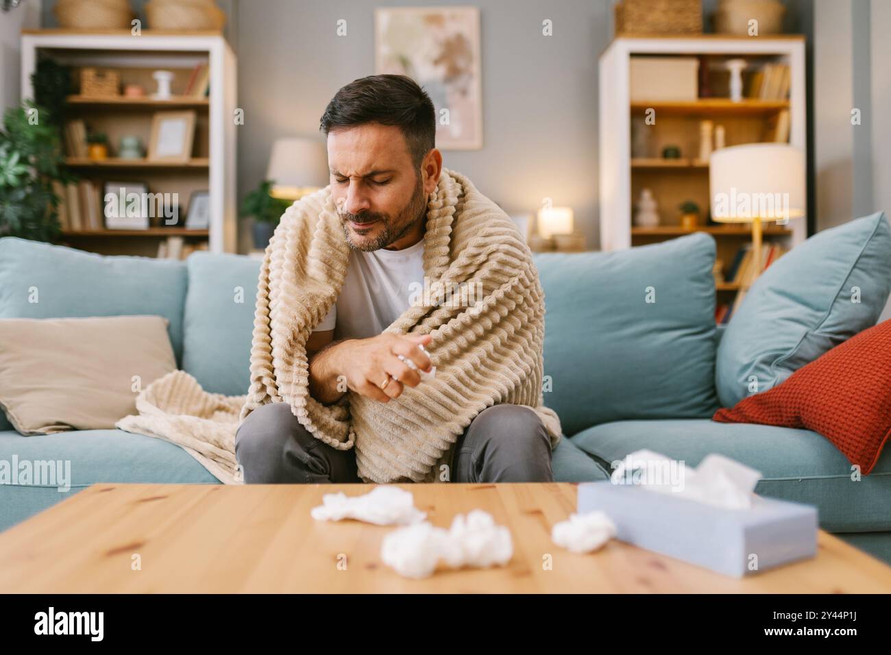 Unwell man covered in a blanket, surrounded by tissues Stock Photo - Alamy