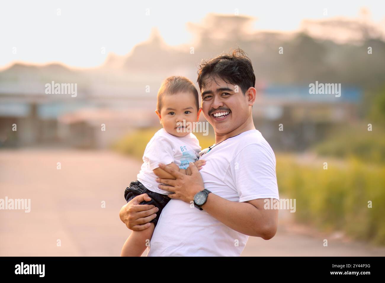The father holds the baby boy warmly and smiles at the camera with the ...
