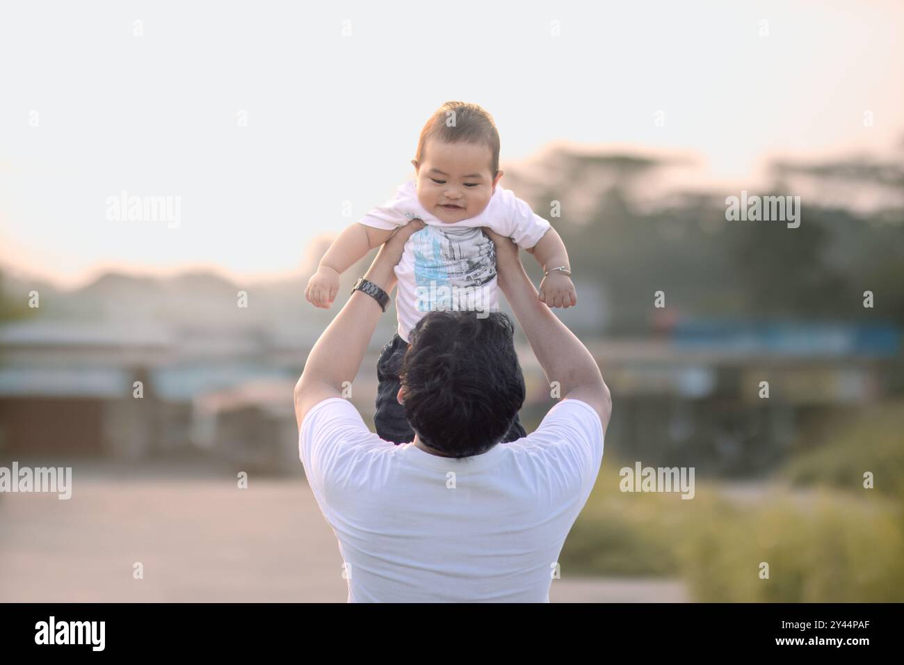 father holding while lifting baby boy. Dad's back is to the camera ...
