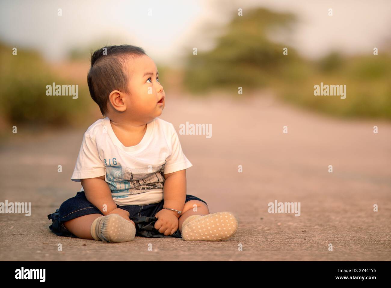 cute asian baby sitting on the road. baby boy facing sideways wearing ...