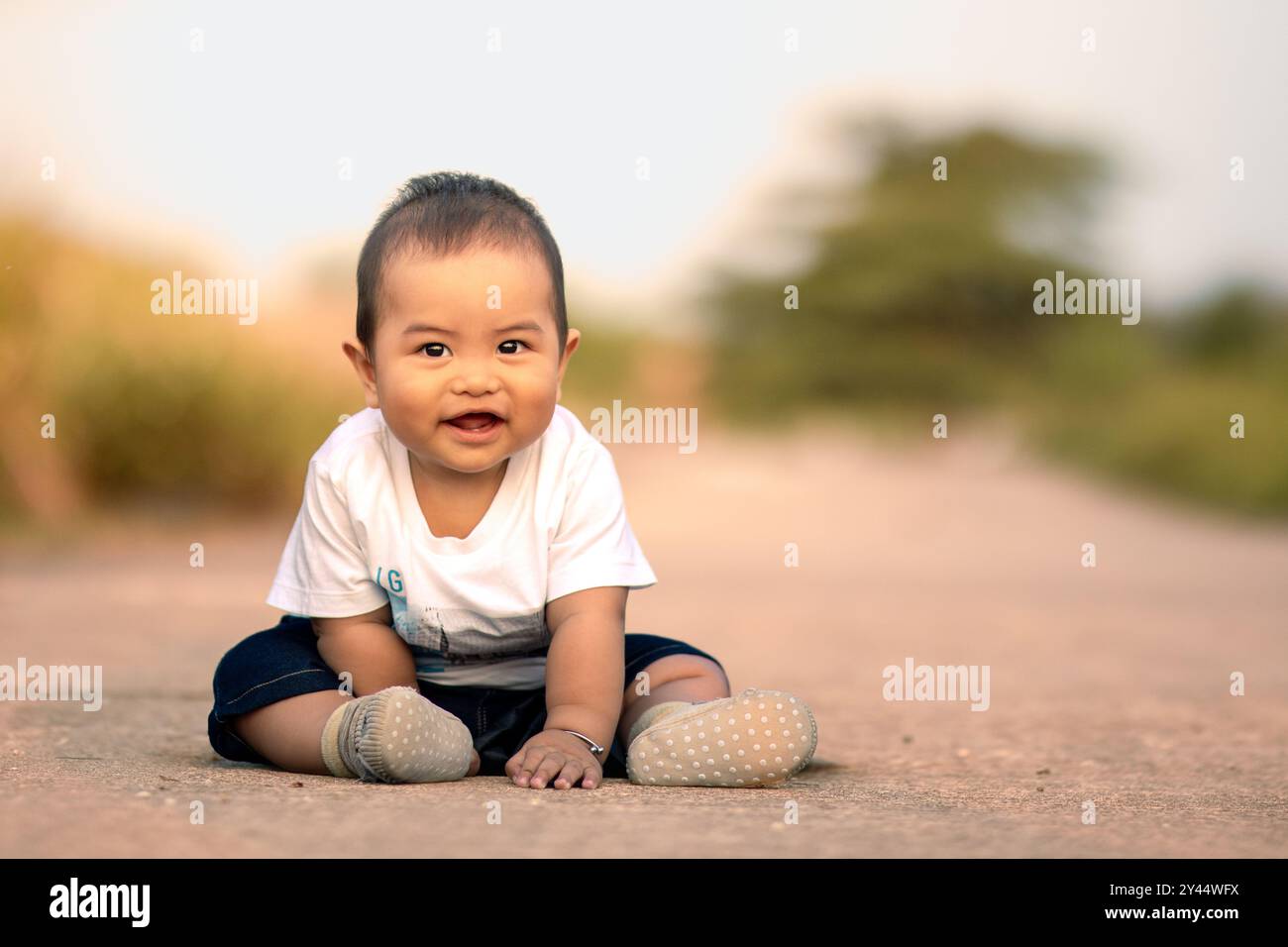 cute asian baby sitting on the road. baby boy facing the camera smiling ...