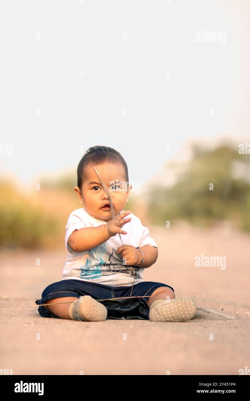 cute asian baby sitting on the road. baby boy holding wild grass while ...