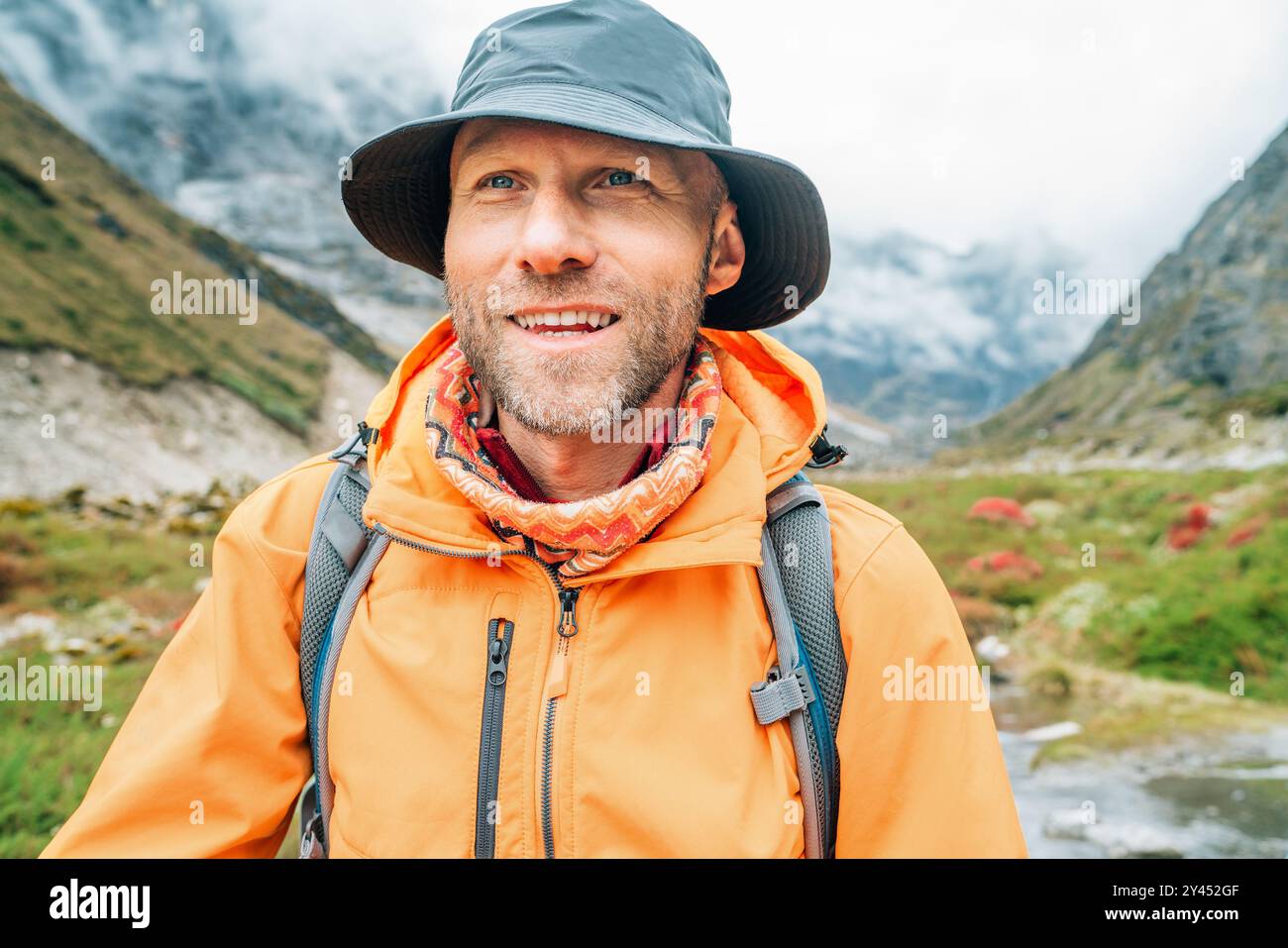 Portrait of smiling Man with backpack dressed orange waterproof jacket ...