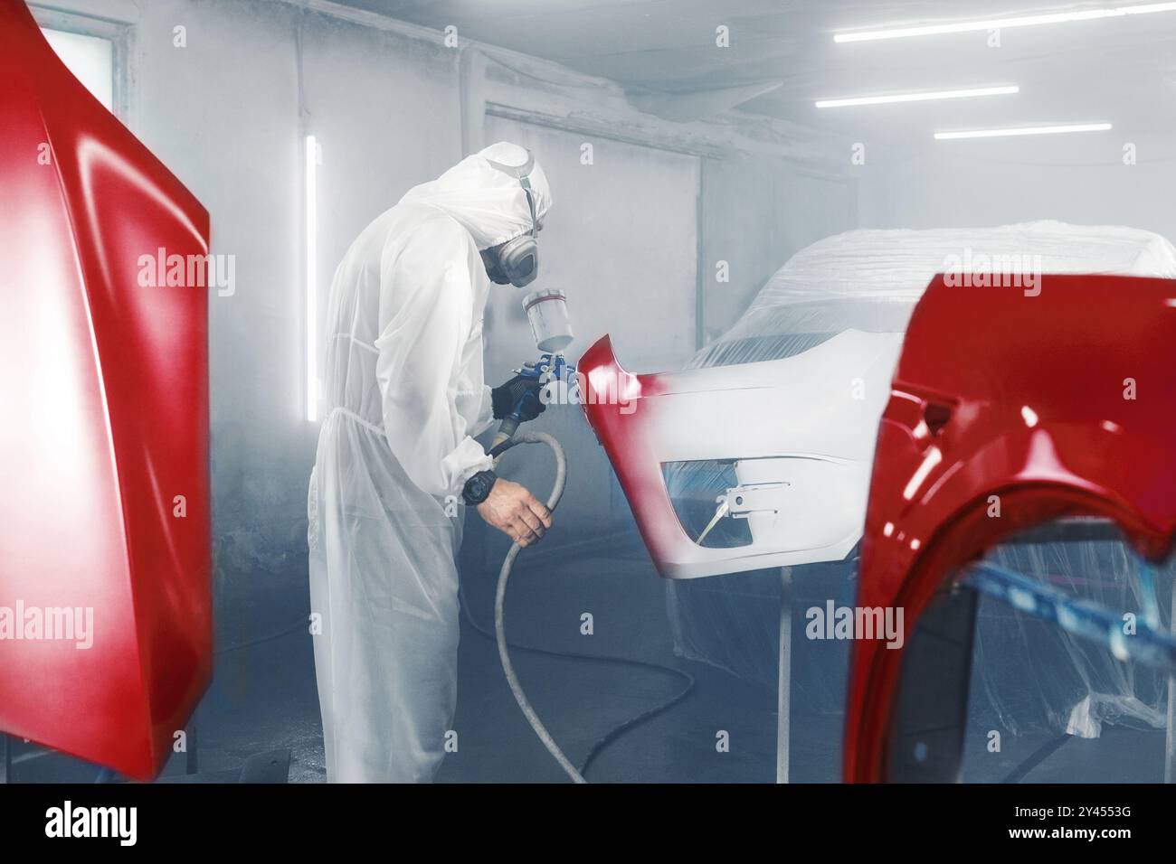 Car paint worker spraying red paint to car body element using spray gun ...