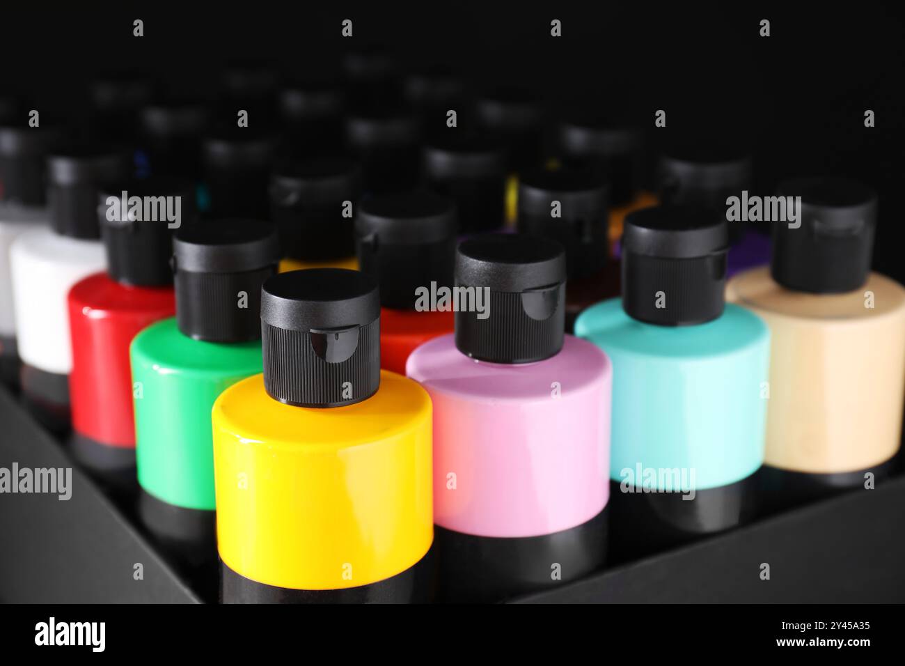 Acrylic paints of different colors in bottles against black background ...