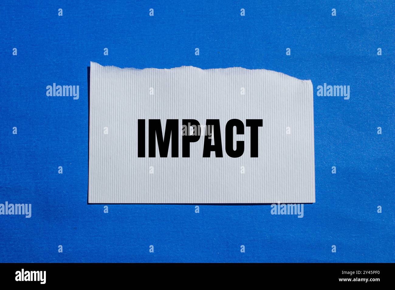 Impact word written on ripped white torn paper piece with blue ...