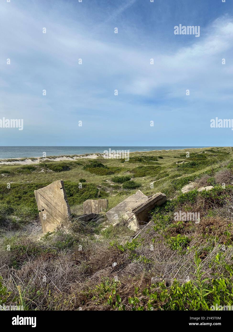 Ruins of a WW2 bunker in grass covered sand dunes and ocean under a ...