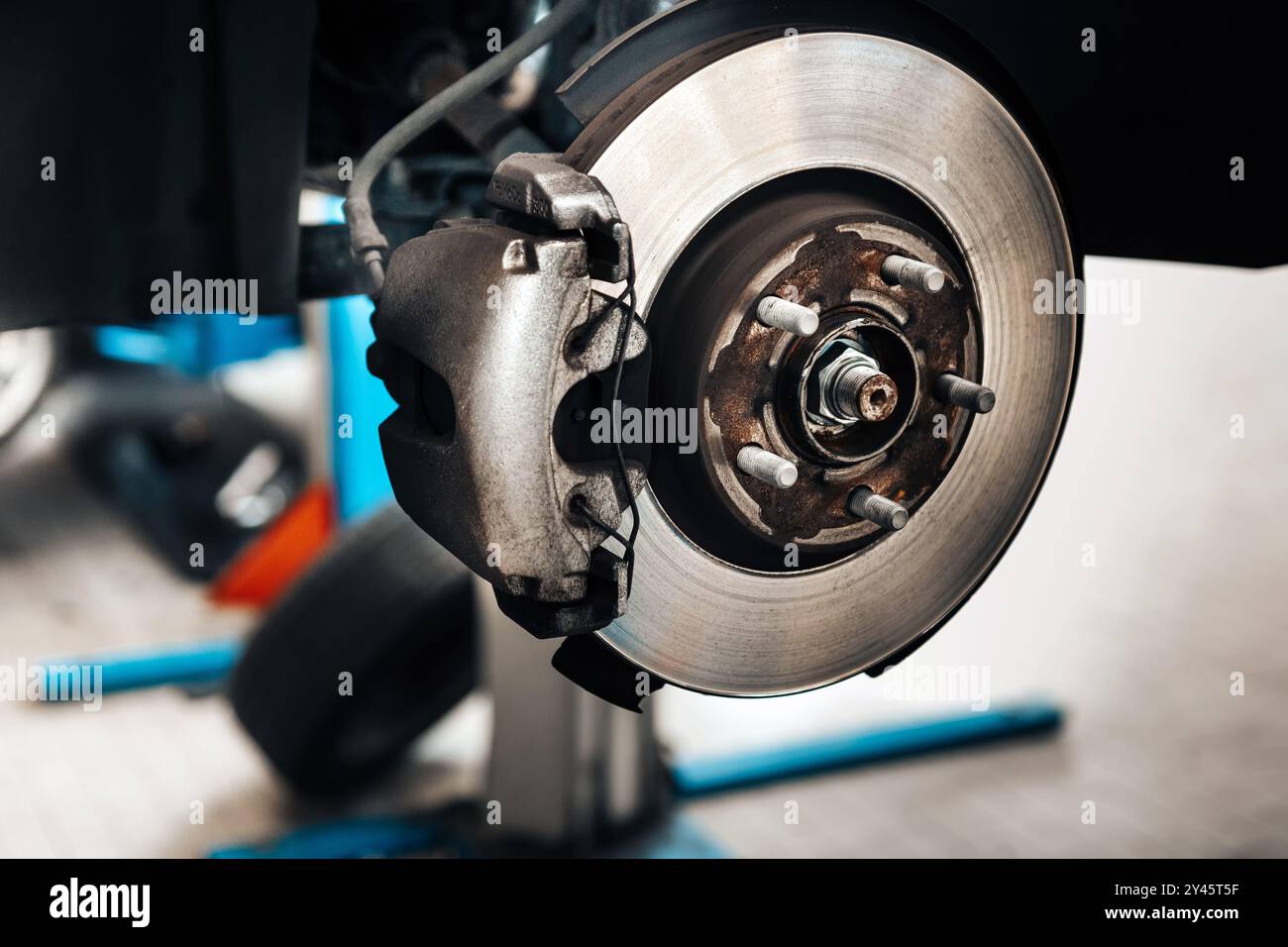 Close up of a car disk brake being repaired in a workshop, showing the brake caliper, rotor, and ...