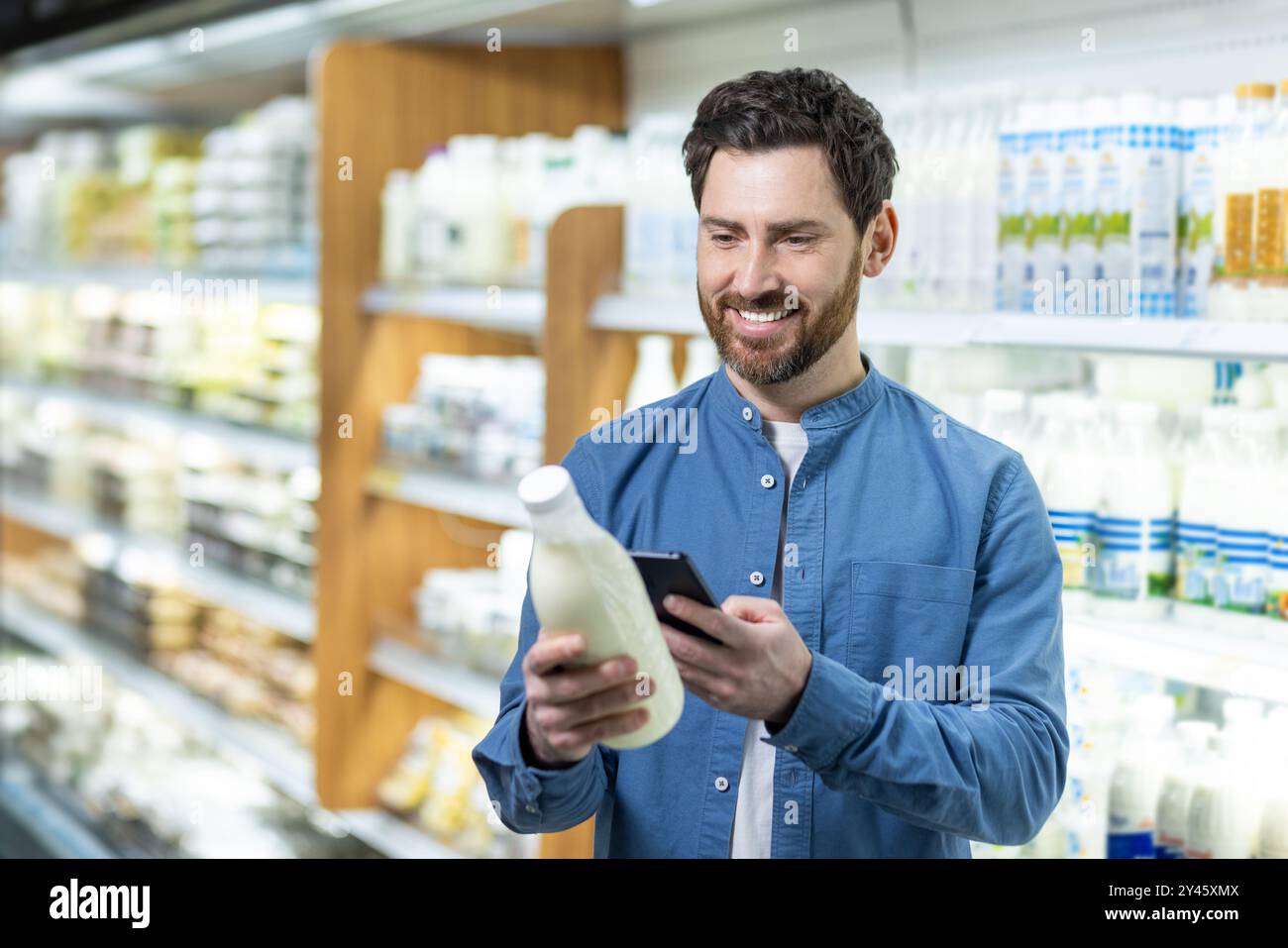 Man in grocery store aisle holding bottle of milk while using ...